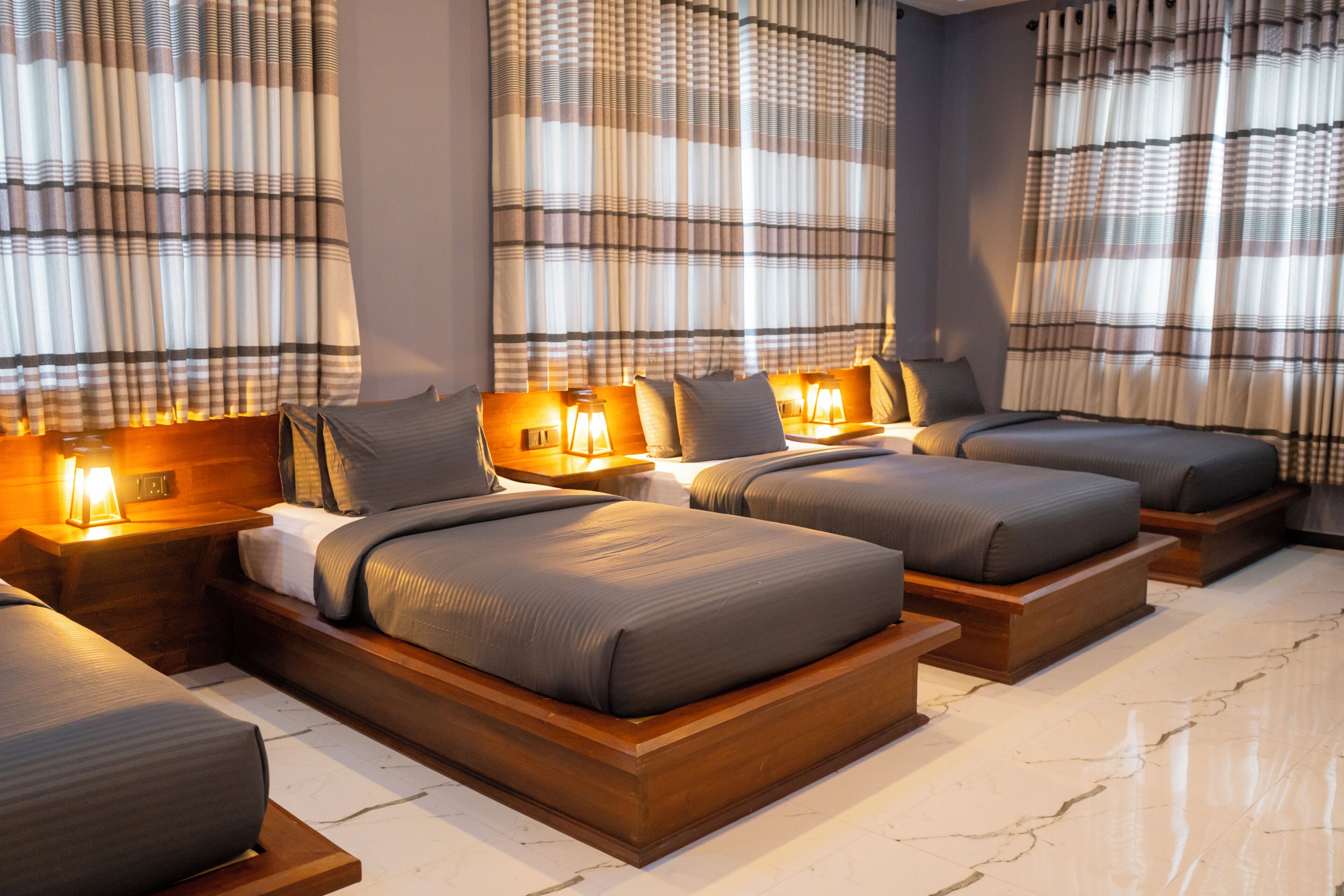 Quarto de hotel com três camas, cabeceiras de madeira e abajures.
