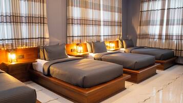 Quarto de hotel com três camas, cabeceiras de madeira e abajures.