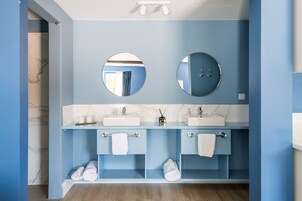 Casa de banho com duas pias, bancadas de mármore e dois espelhos redondos.