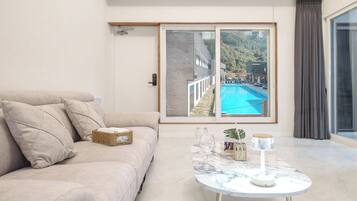 Uma sala de estar moderna com sofá, mesa de centro e uma grande janela com vista para uma piscina.