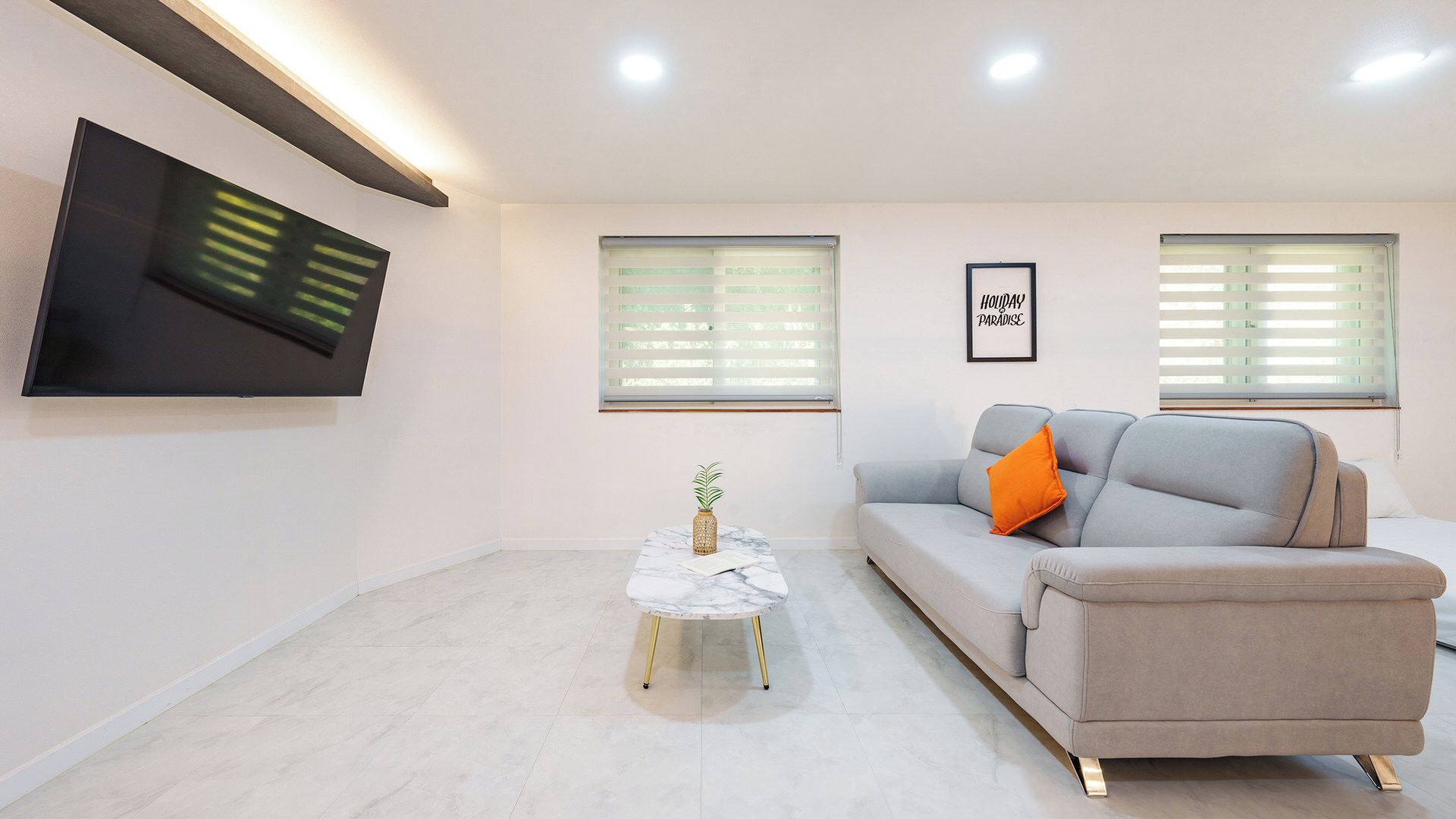 Uma sala de estar moderna com um sofá cinzento, uma pequena mesa de centro branca com uma planta e um quadro na parede.