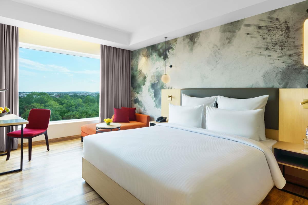 Quarto de hotel com uma cama grande, uma escrivaninha com cadeira, vista para o exterior e parede com textura.