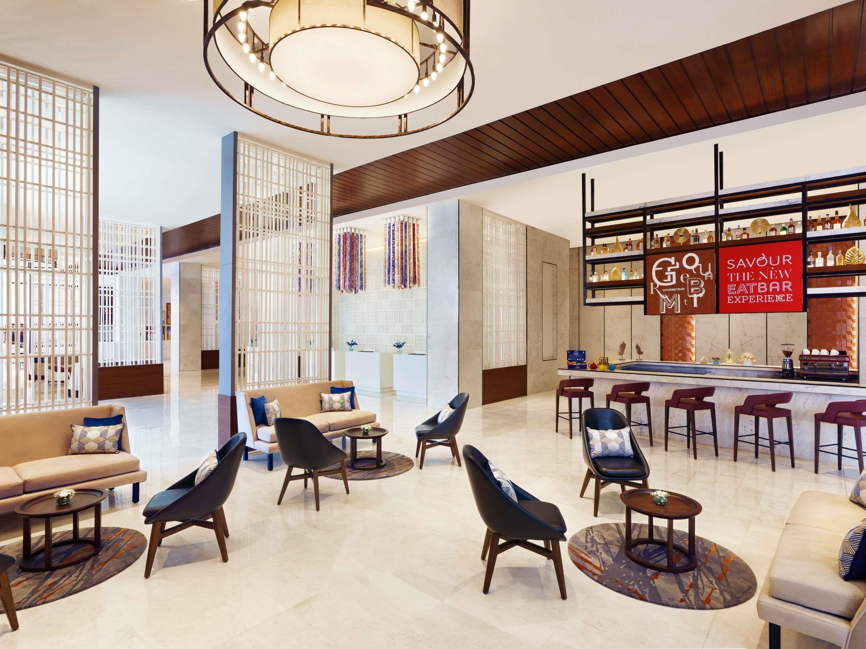 Uma área de bar moderna com teto alto e um candelabro central, rodeada por assentos e uma exibição de garrafas.