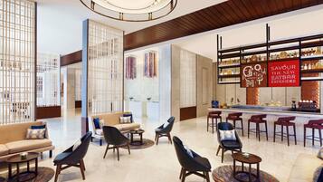 Uma área de bar moderna com teto alto e um candelabro central, rodeada por assentos e uma exibição de garrafas.
