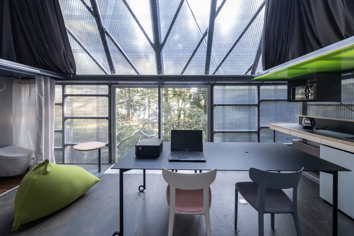 Um interior moderno com uma janela ampla, um laptop sobre uma mesa e um pufe verde.