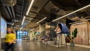 Um espaço interior moderno com teto alto, tubulações expostas e uma variedade de áreas de estar.
