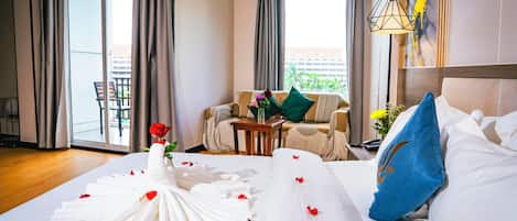 Quarto de hotel com uma cama grande, um sofá, uma mesa com um vaso de flores e vista para o exterior.