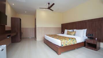 Quarto de hotel com cama, mesa de cabeceira, escrivaninha e ventilador de teto.