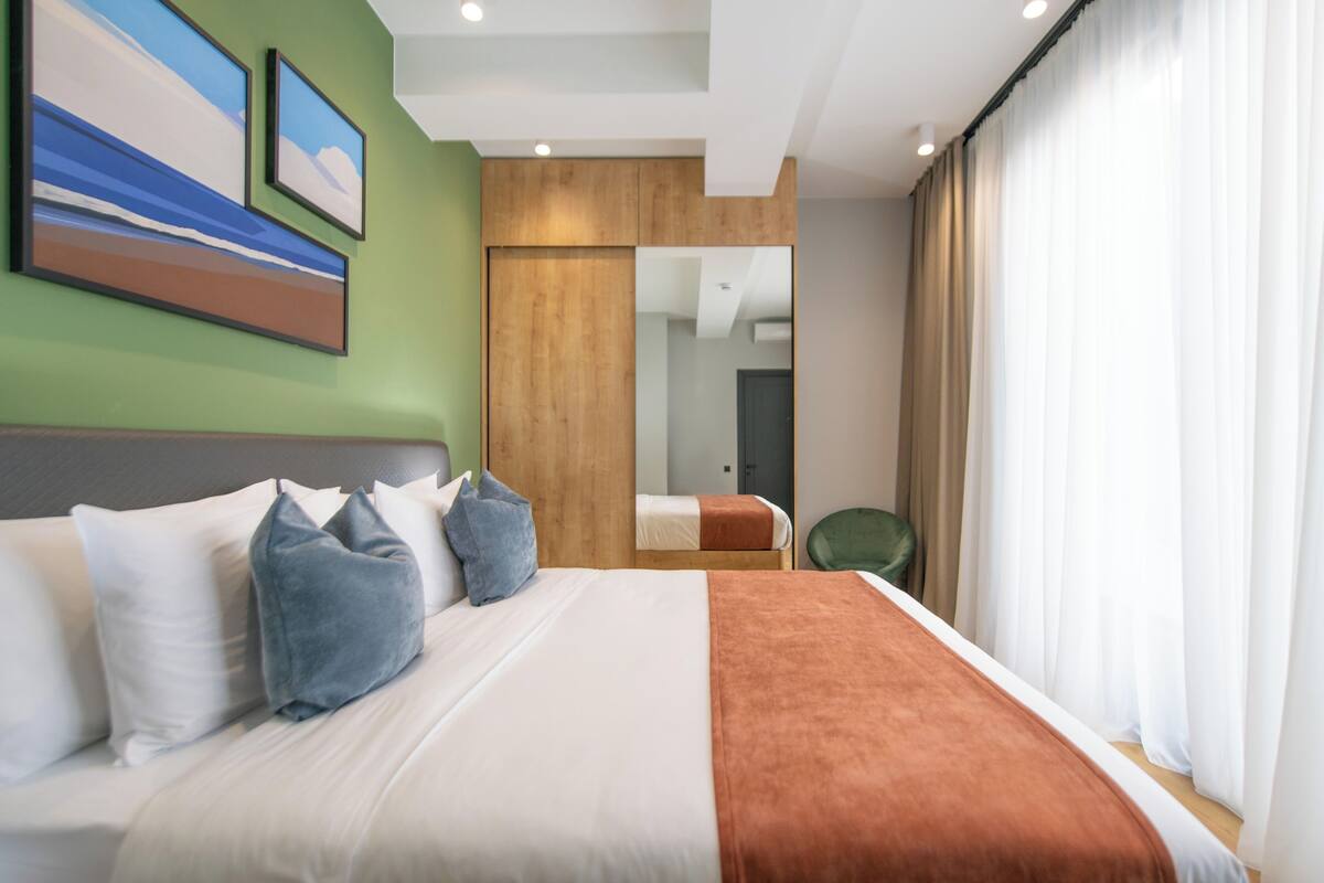 Quarto de hotel moderno com uma cama grande, uma parede verde de destaque e obras de arte.