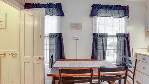 Uma sala de jantar com mesa e cadeiras de madeira, uma porta branca e janelas com cortinas azuis.