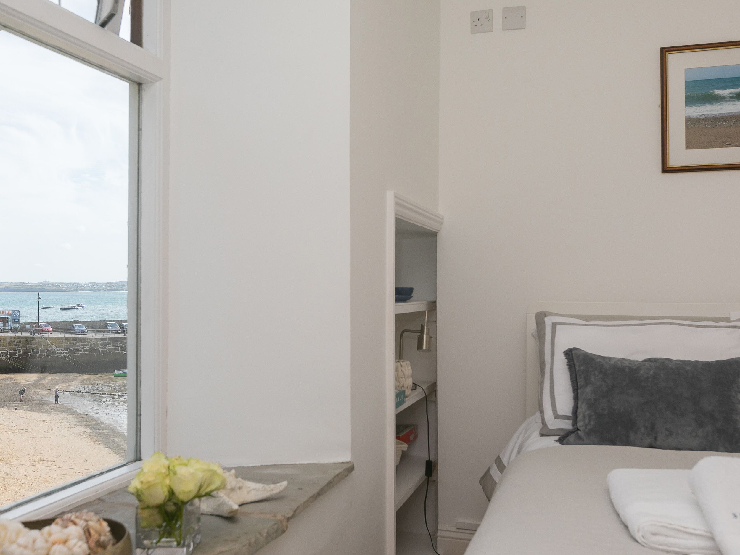 Quarto com cama, janela vista para o mar e prateleira com objetos.