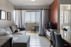 Uma sala de estar moderna com sofá, mesa de jantar, cadeiras, TV e varanda com cortinas.