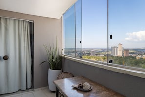 Varanda com vista para a paisagem urbana, um vaso de planta, uma mesa de jantar com um prato e uma porta de correr.