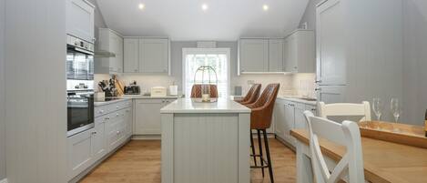 Cozinha moderna com armários brancos, uma ilha central e piso de madeira.