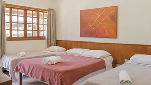 Quarto de hotel com três camas, uma janela grande com cortinas e uma pintura abstrata pendurada na parede.