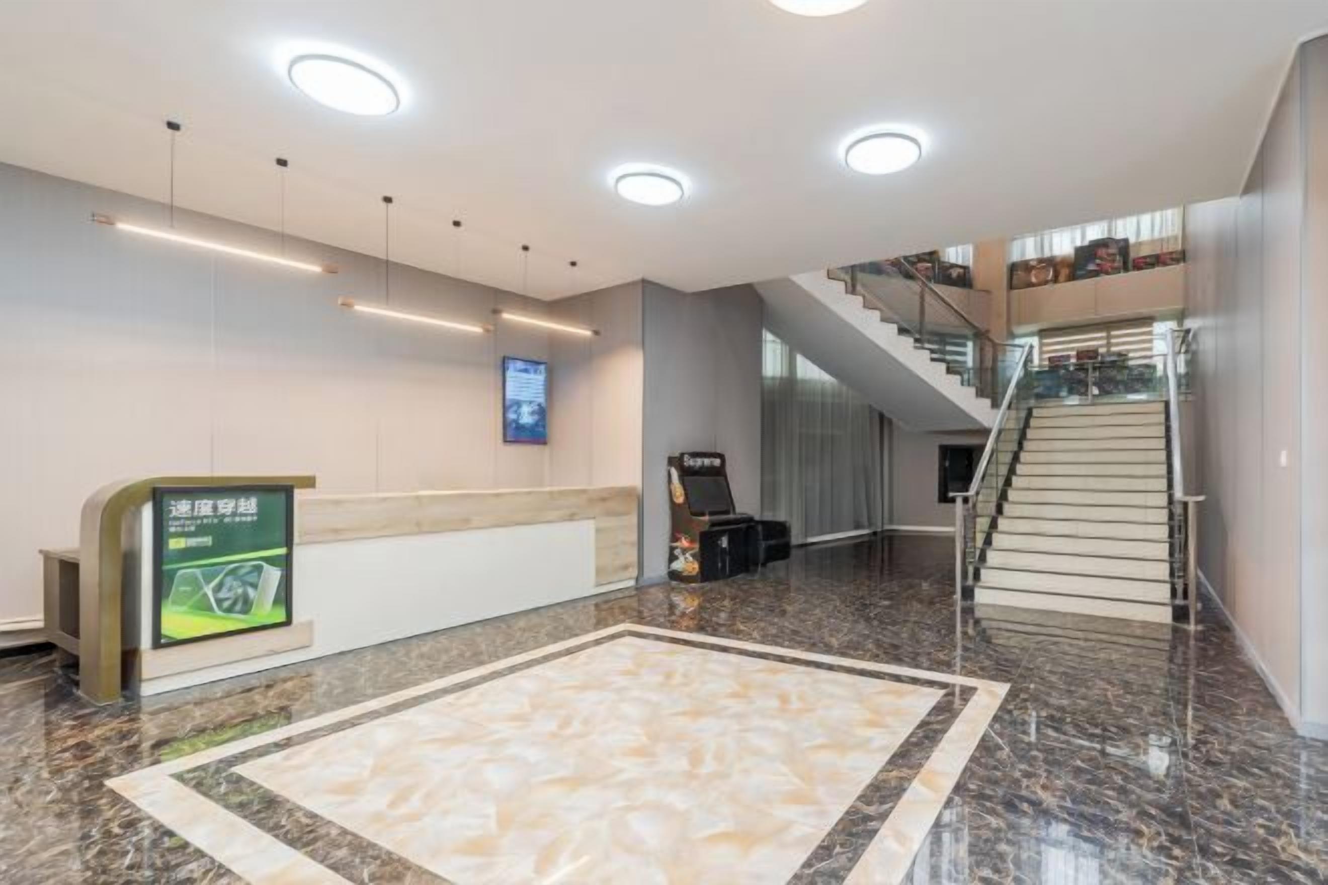 Um saguão de hotel com uma mesa de recepção, uma tela digital, piso de mármore e uma escada.