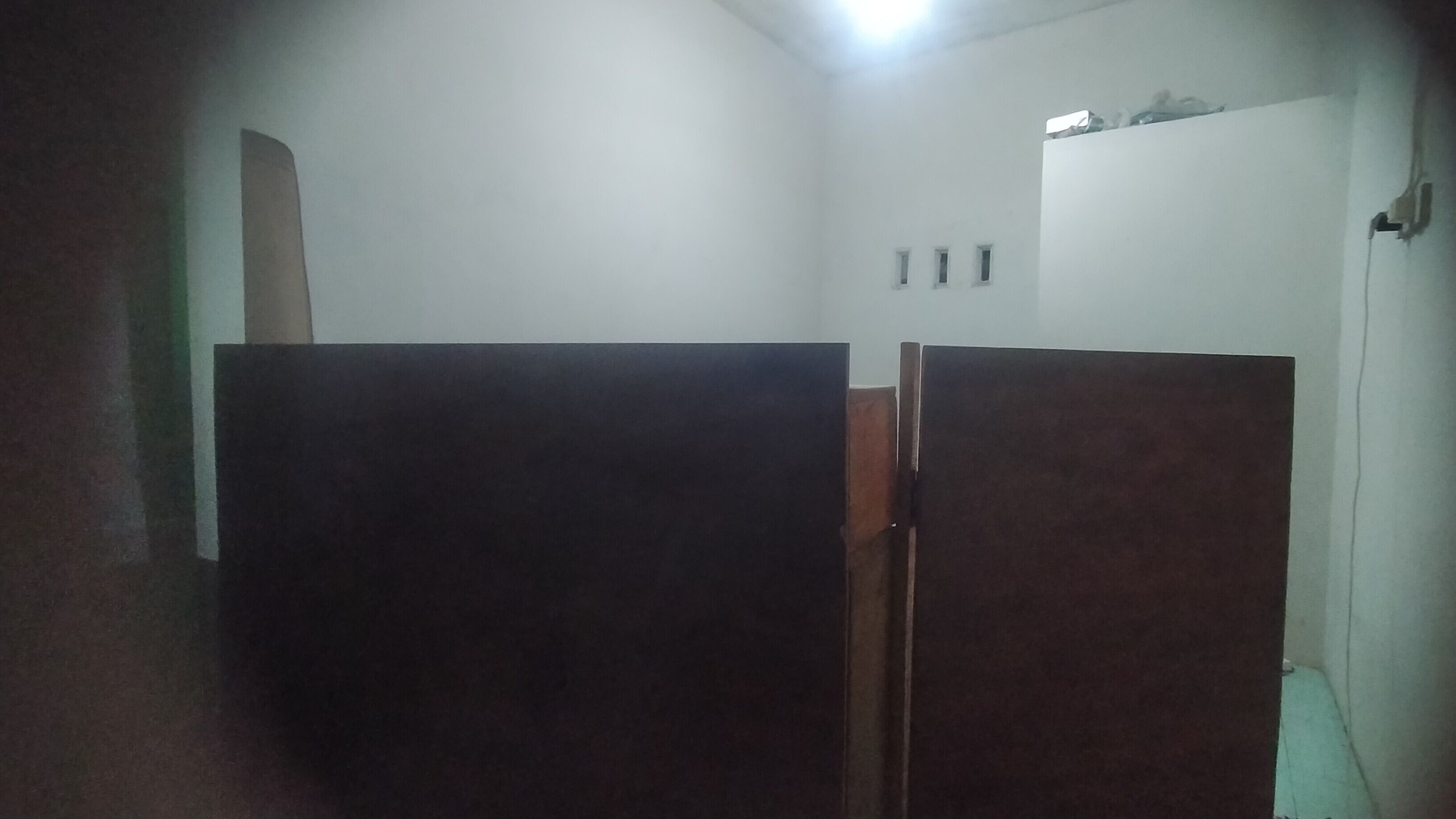 Um quarto pequeno e com pouca luz, com uma única divisória de madeira e uma porta branca.