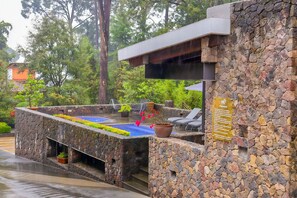 Uma área externa com paredes de pedra, piscina, espreguiçadeiras e uma placa indicando uma câmera de alta definição.