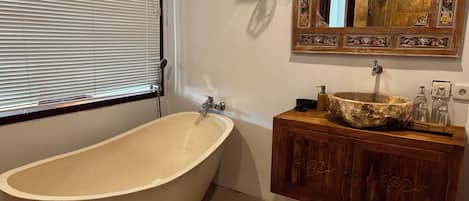 Um banheiro com banheira de pedestal, um lavatório de madeira com pia e um espelho decorativo com moldura floral.
