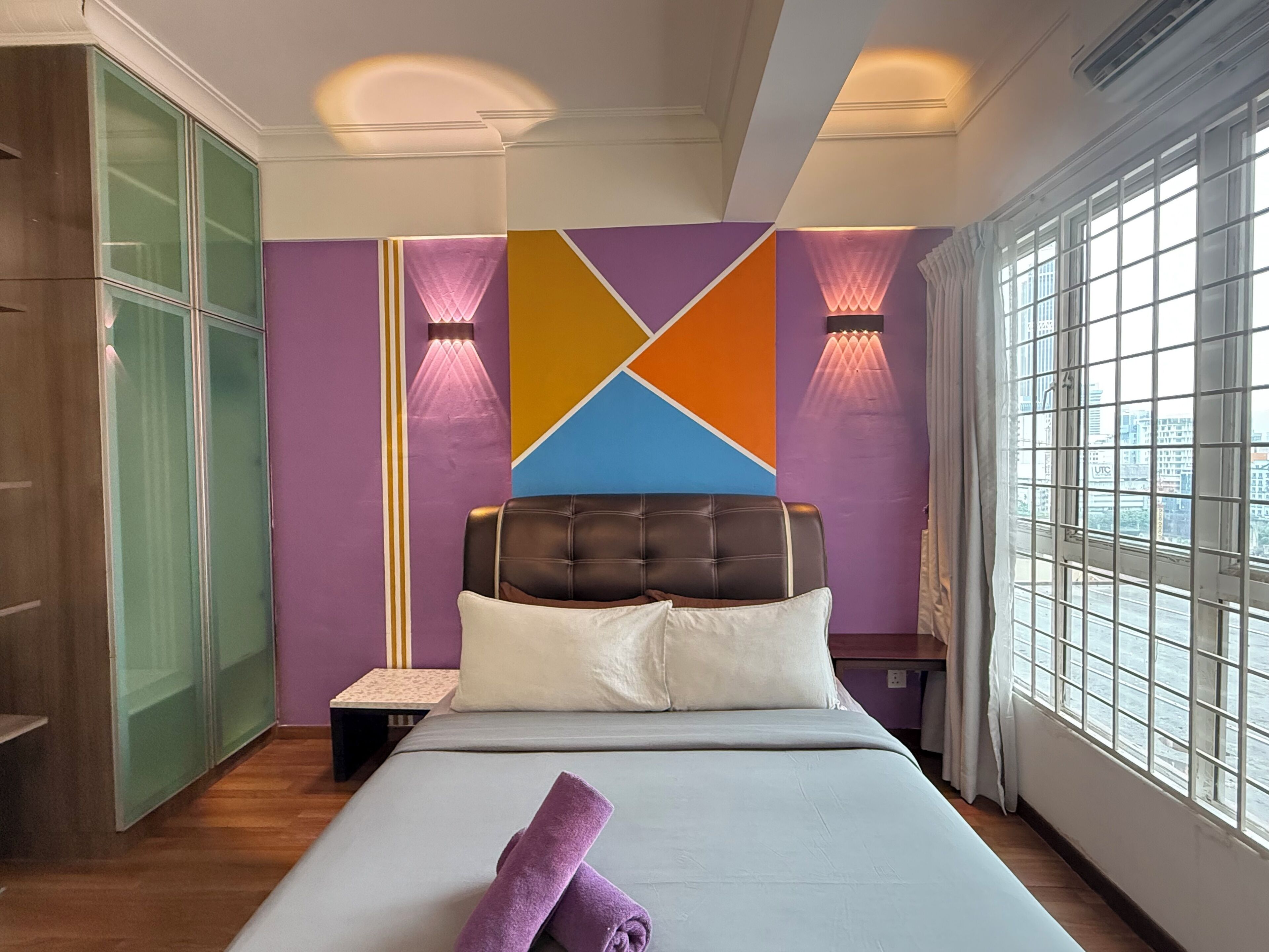 Quarto de hotel com cama, guarda-roupa, mesa de cabeceira e janela com vista para a cidade.