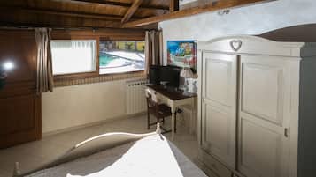 Um quarto com cama, escrivaninha com televisão, guarda-roupa e janela com cortinas.