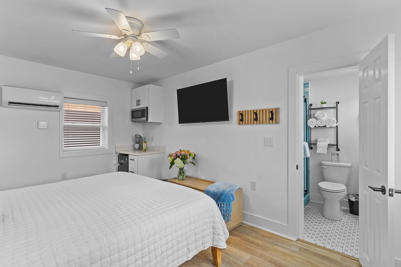 Quarto com cama, ventoinha no teto, televisão, micro-ondas e banheiro visível por uma porta aberta.