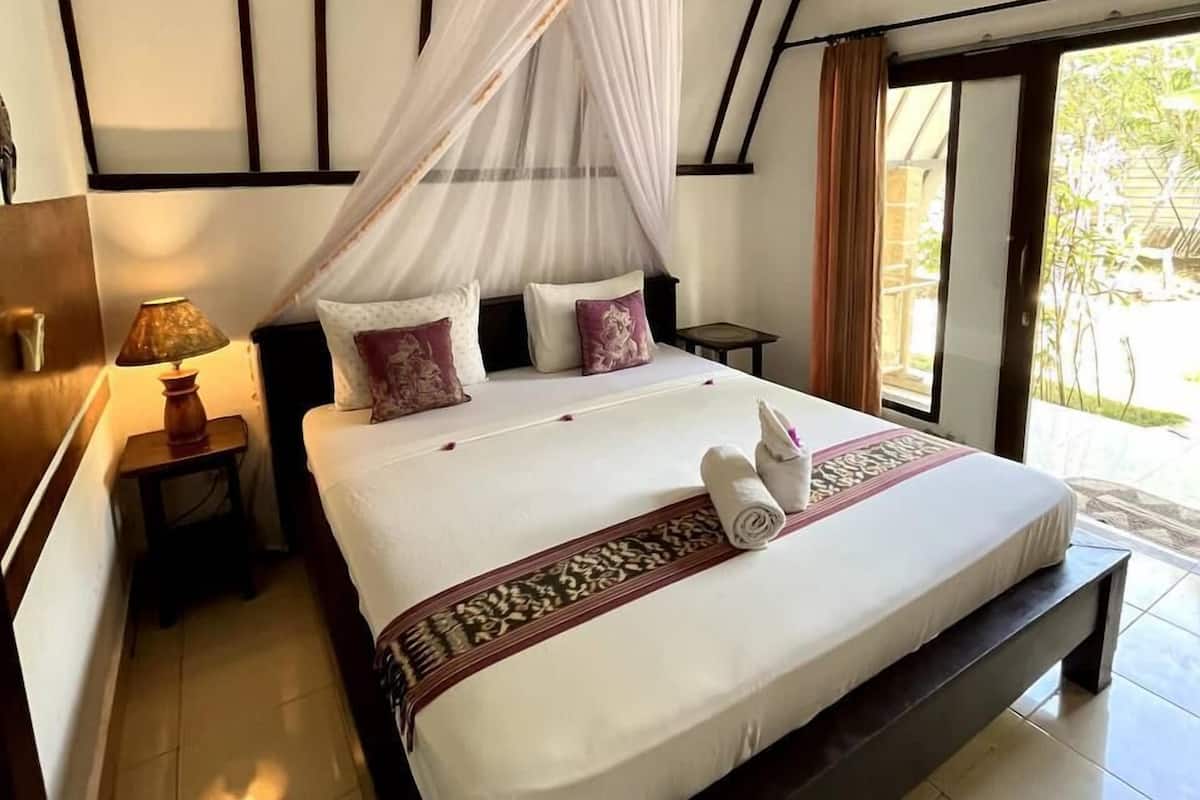 Quarto com cama, mesa de cabeceira, luminária, dossel e vista para o exterior.