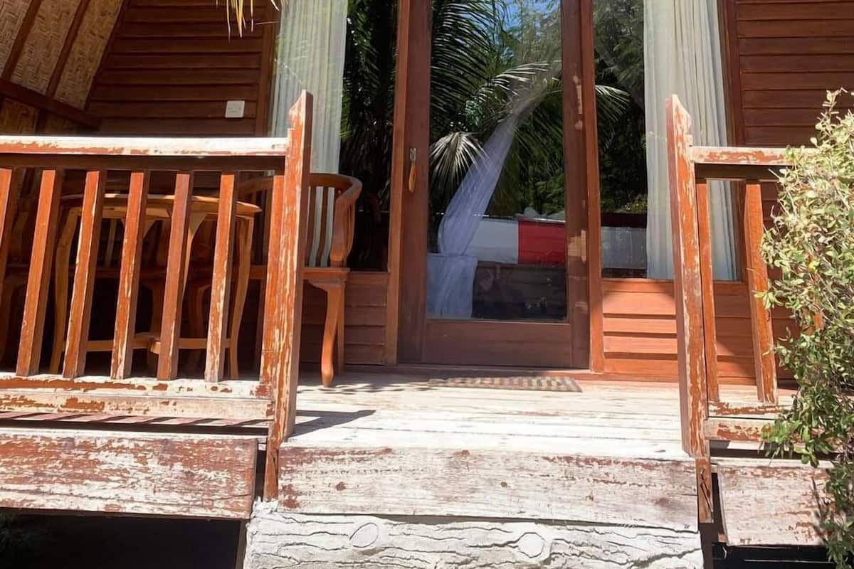 Uma cabana de madeira com telhado de palha, um alpendre de madeira com bancos, e uma porta com o número 6.