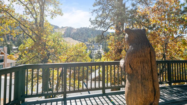 Escultura de urso de madeira em um deck de madeira, com vista para uma paisagem montanhosa.