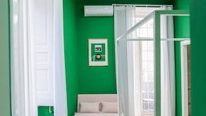 Quarto com cama, sofá, mesinha e janela com cortinas.