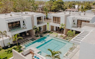 Um edifício moderno de vários andares com piscina no terraço, área de estar externa e paisagismo exuberante.