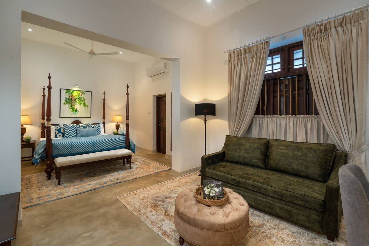 Quarto com uma cama de dossel, um sofá verde e um banquinho redondo.