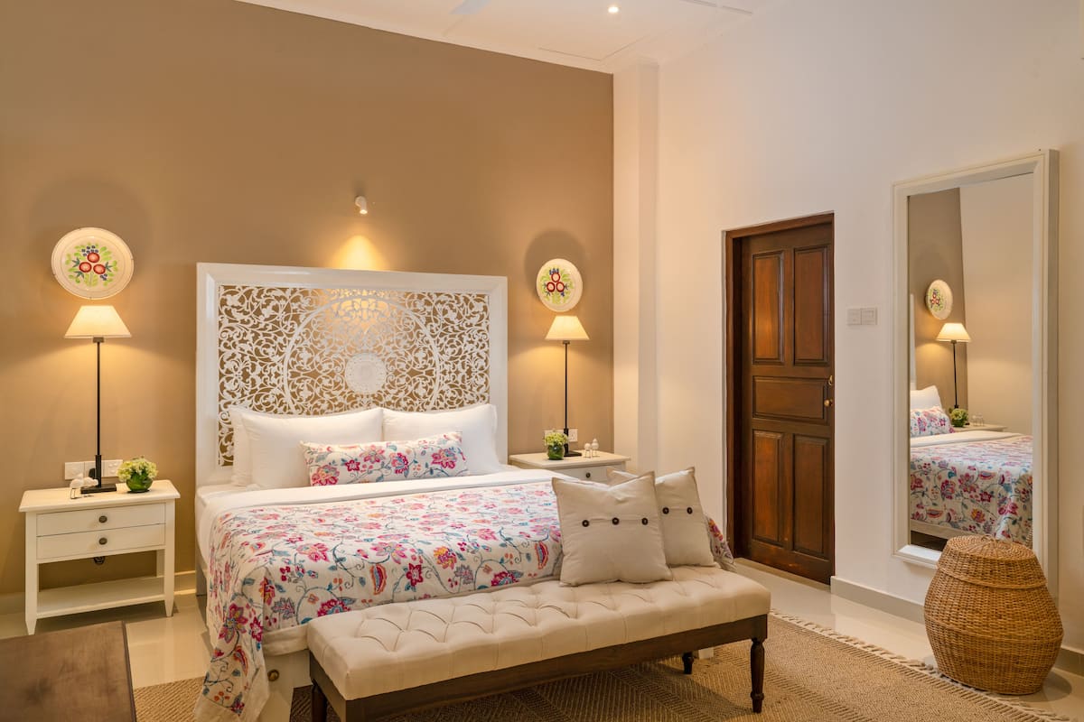 Quarto com cama grande, duas mesas de cabeceira, painel de cama decorativo e um espelho.