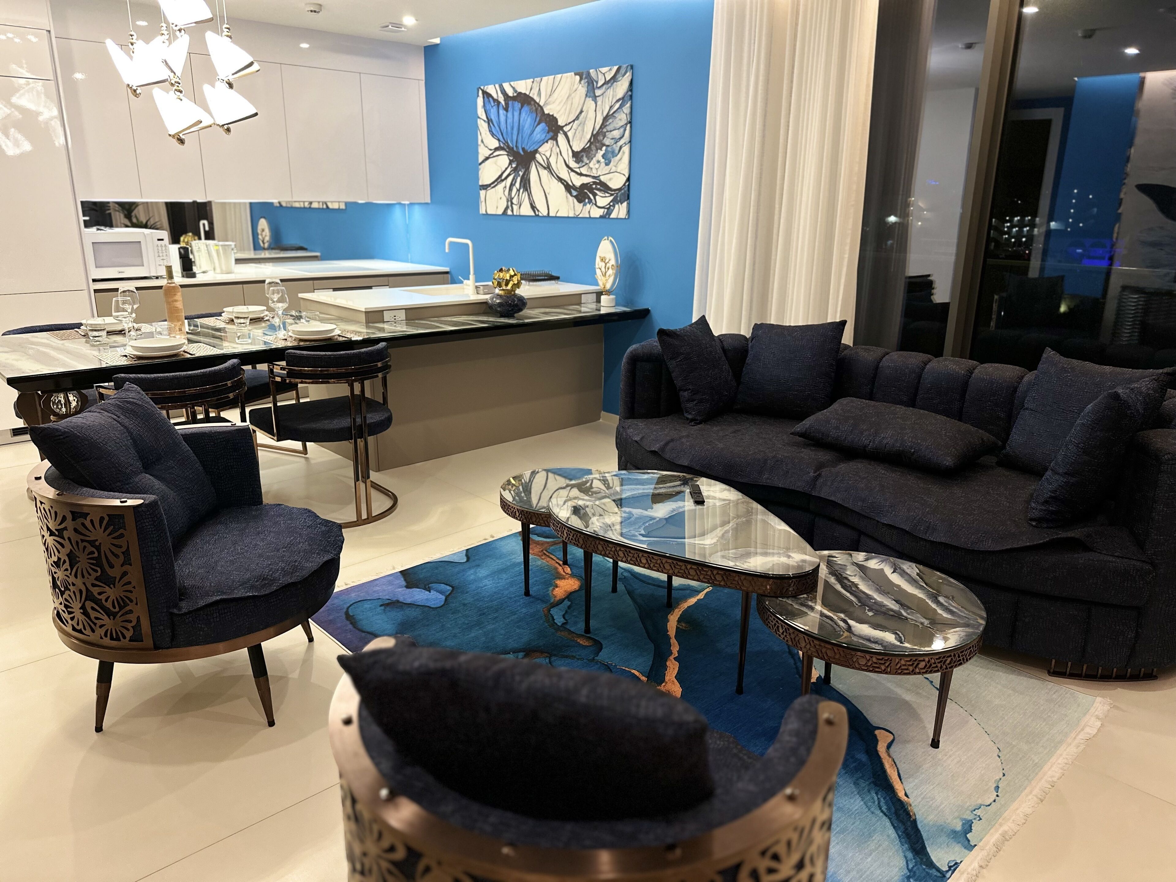 Uma sala de estar moderna com uma parede azul de destaque, um sofá, uma mesa de centro e uma área de jantar com mesa e cadeiras de vidro.