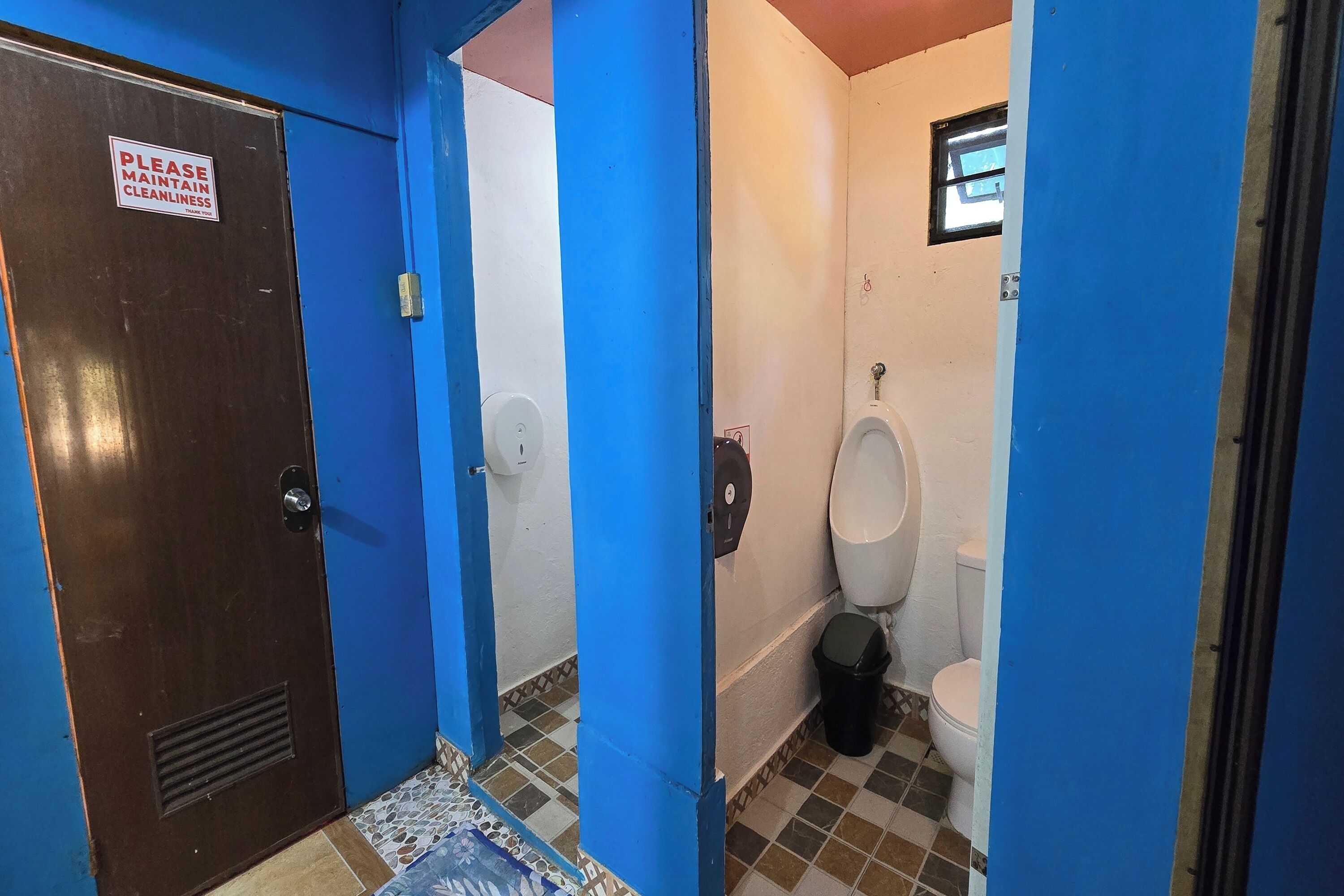Um corredor estreito com uma porta azul, uma placa solicitando manter a limpeza e um banheiro com dispensador de papel toalha.