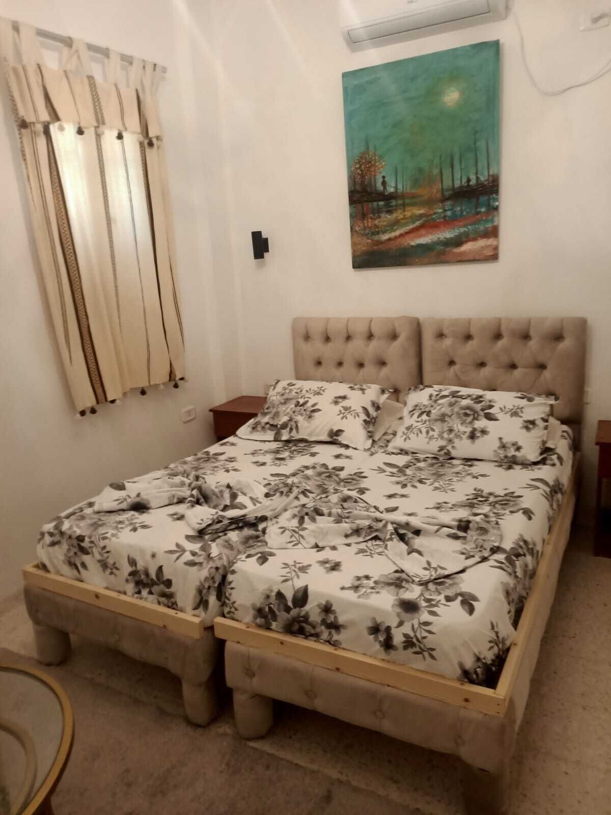 Quarto com cama, um quadro na parede e janela com cortinas.