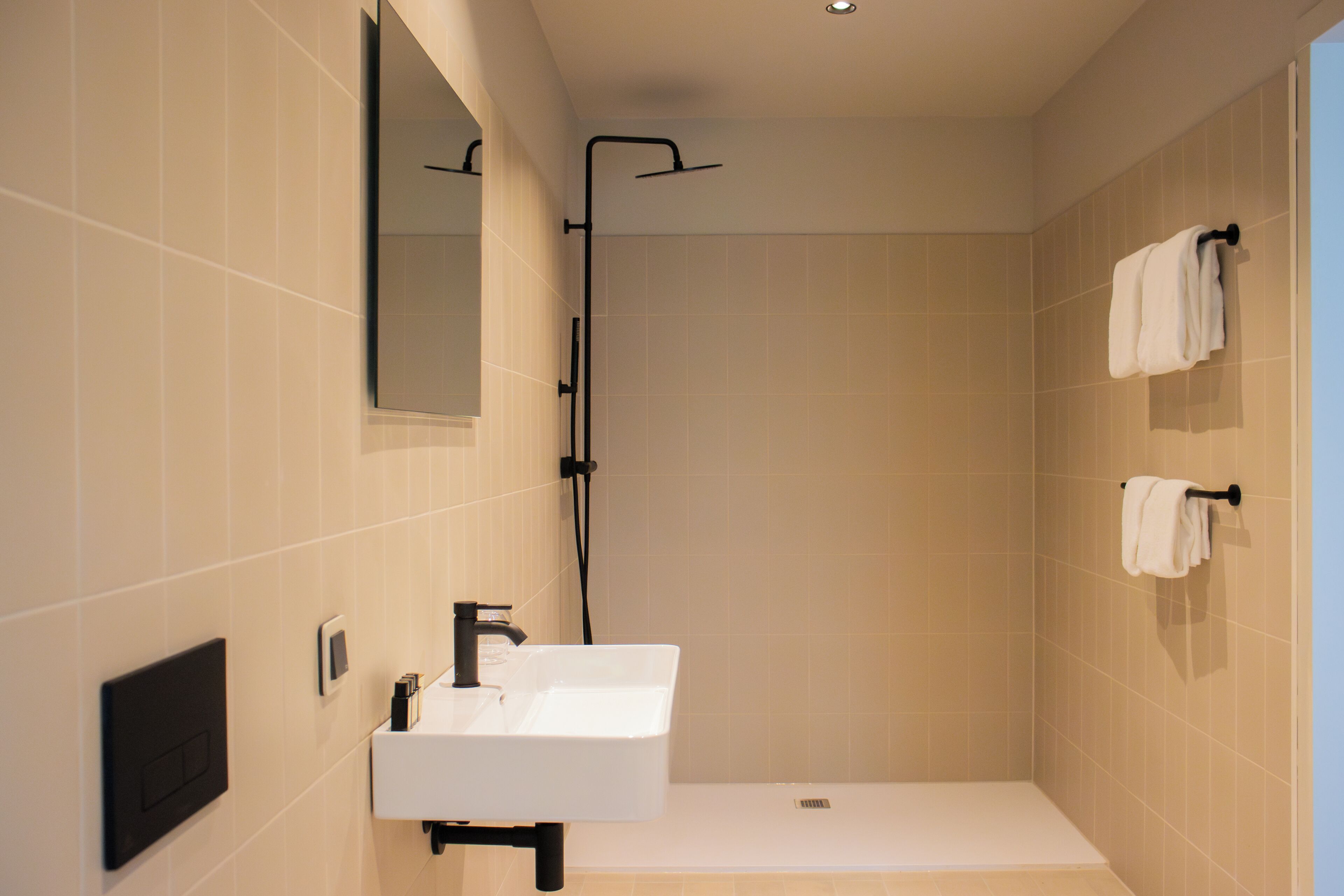 Casa de banho moderna com lavatório branco, chuveiro manual e suporte para toalhas.
