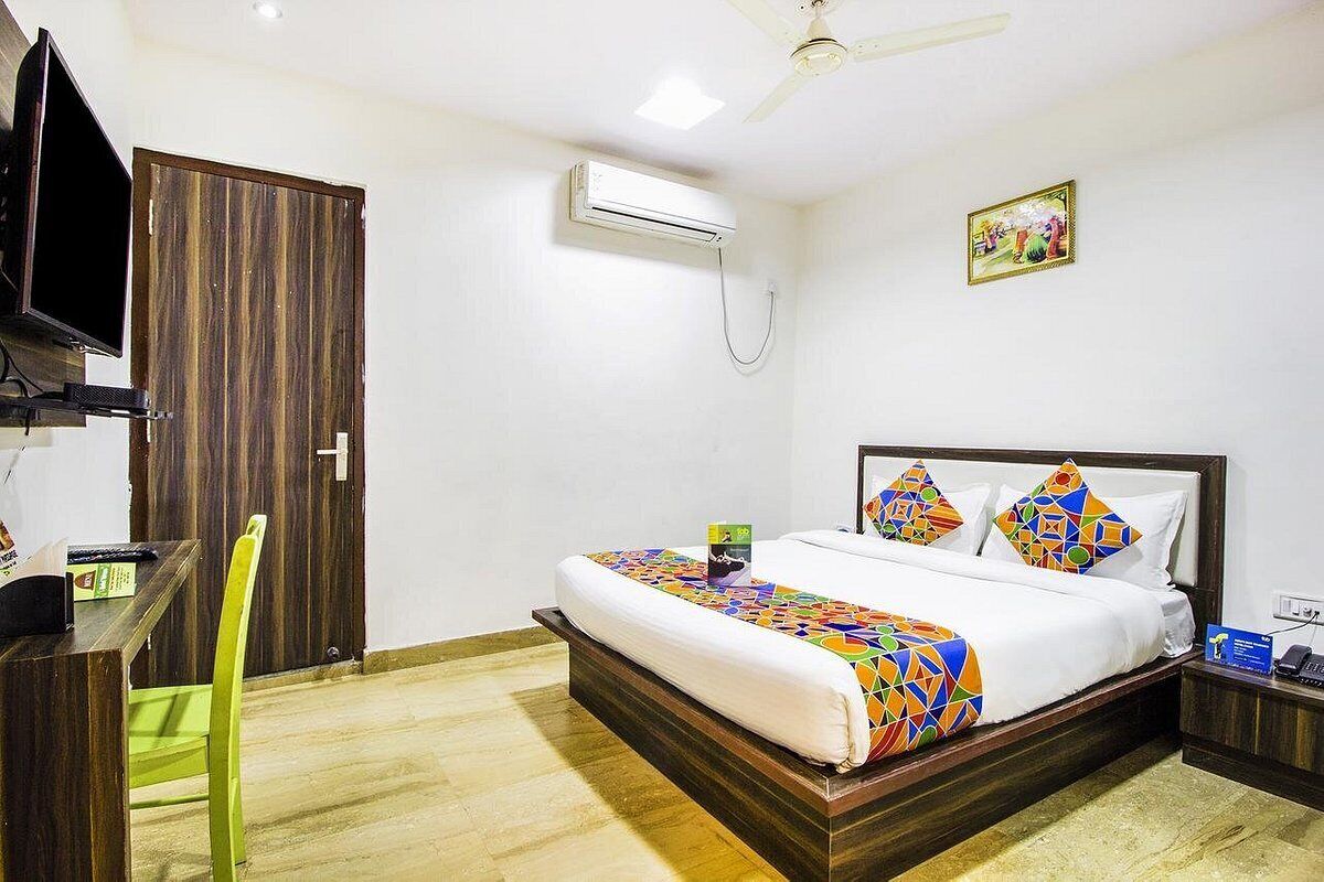 Quarto de hotel com cama, escrivaninha, cadeira, ar condicionado, ventoinha no teto e um quadro na parede.