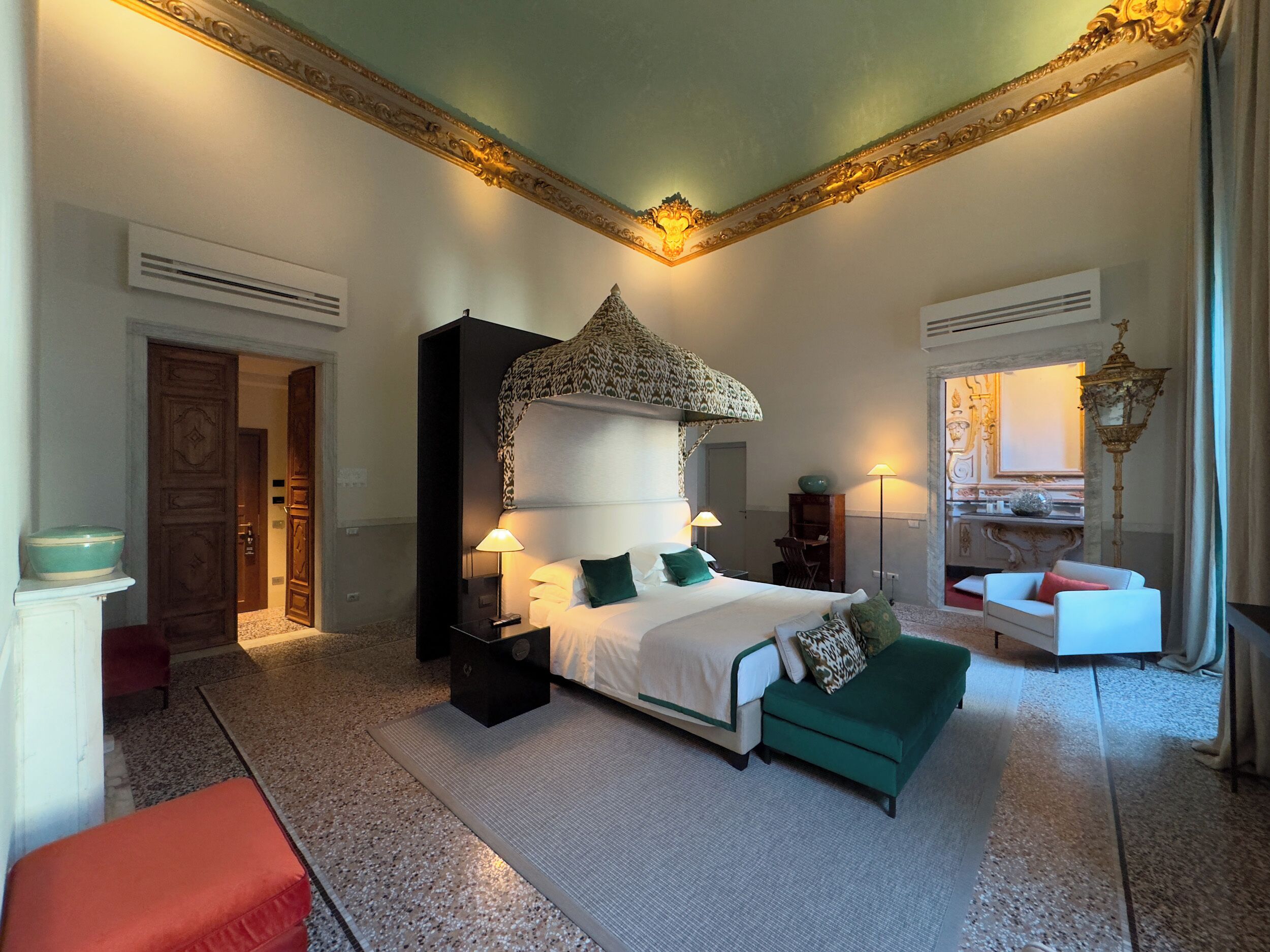 Um quarto espaçoso com uma cama grande, um sofá verde e uma área de estar separada.