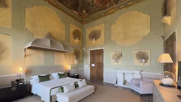 Quarto de hotel com cama grande, escrivaninha, cadeira, lareira e um mural no teto.