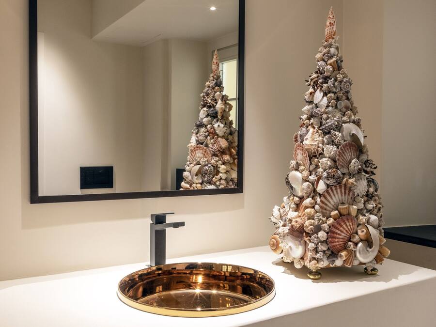 Casa de banho com lavatório branco, um espelho grande e um arranjo decorativo de conchas.