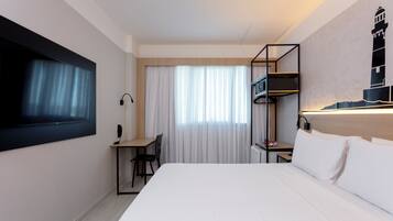 Quarto de hotel com uma cama, uma escrivaninha, uma cadeira, uma televisão e um quadro de um farol.