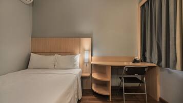 Quarto de hotel com cama, escrivaninha, cadeira e telefone.