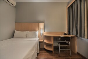 Quarto de hotel com cama, escrivaninha, cadeira e telefone.