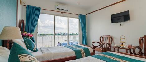Quarto de hotel com duas camas, uma televisão, uma cadeira, uma mesa e vista do céu através de grandes janelas.