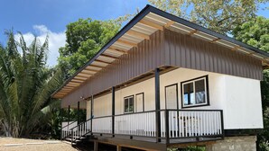 Uma casa moderna com varanda coberta, base de concreto e vista para o verde ao redor.