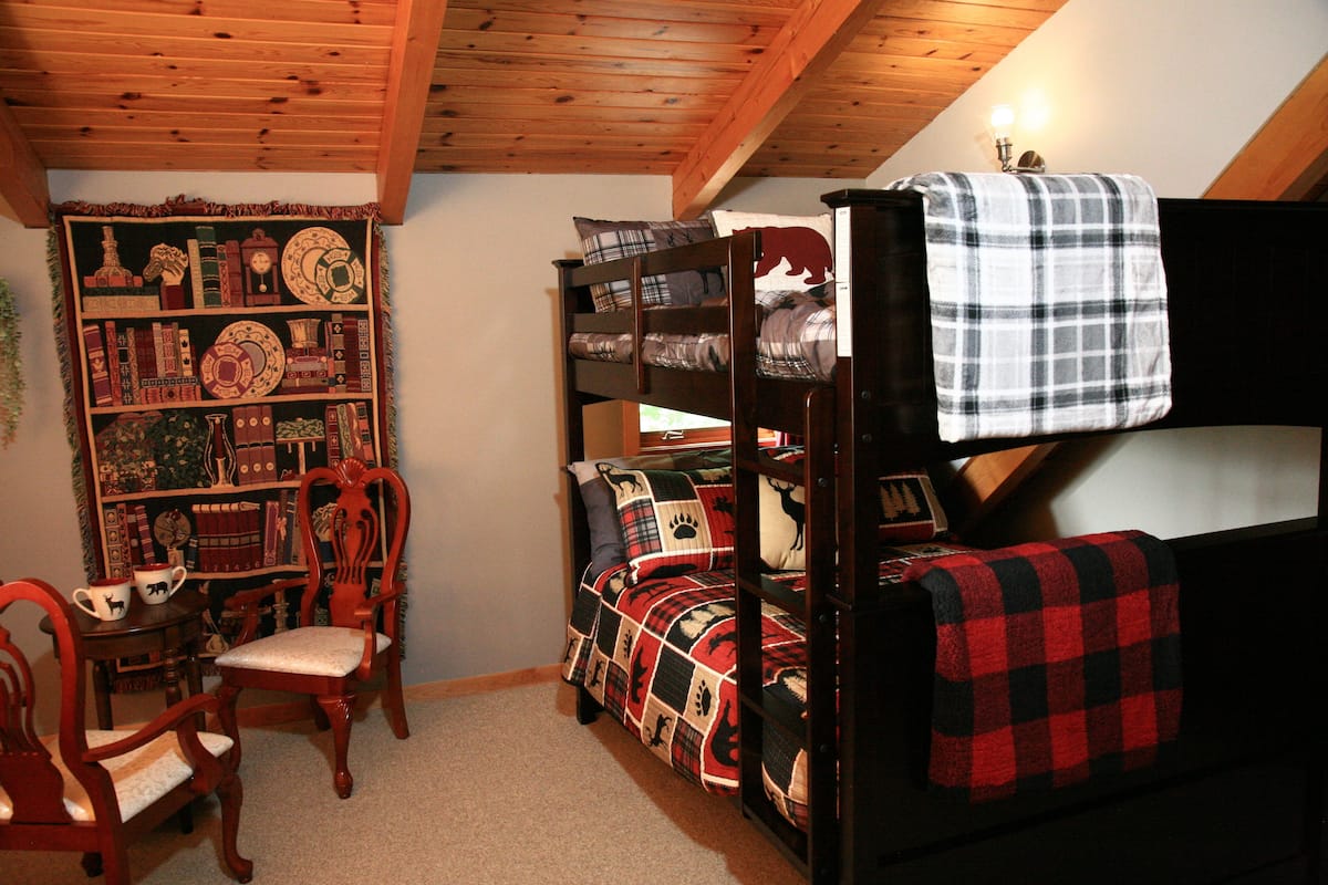 Um quarto aconchegante com uma cama beliche, uma estante de madeira e uma área de refeições com cadeiras.