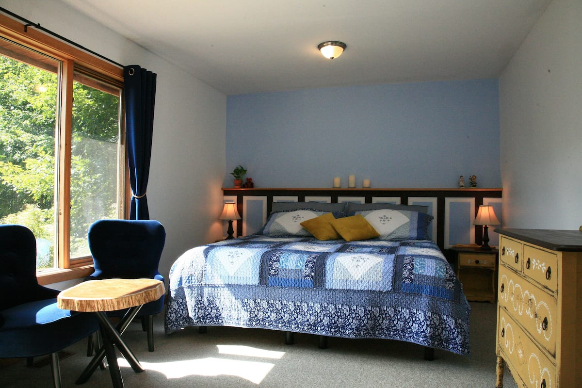 Quarto com uma cama, duas cadeiras, cômoda e janela com cortinas.