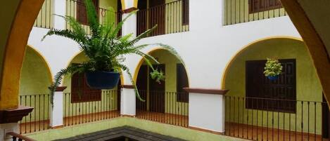 Um pátio com planta suspensa central, várias sacadas e uma porta azul.