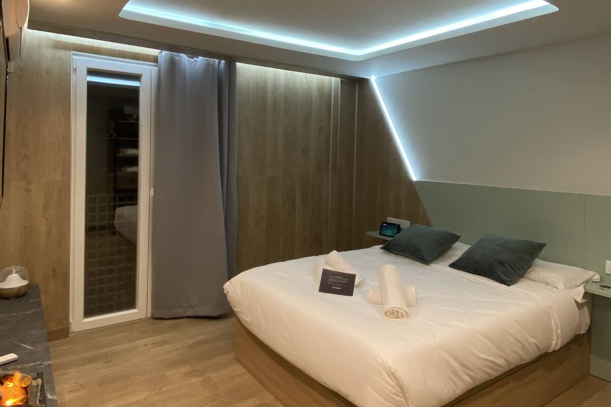 Quarto de hotel moderno com uma cama grande, uma mesa de cabeceira, lareira embutida e luminária no teto.
